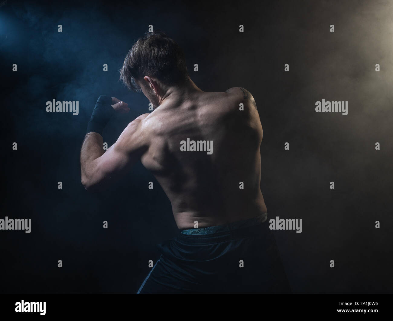 A young handsome bearded male shadow boxes in a dark and smoke filled ...