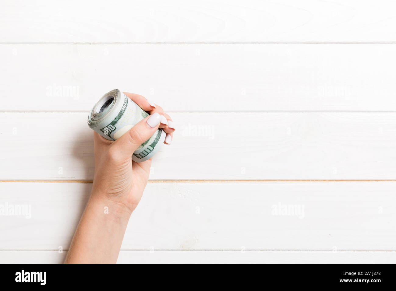 Female hand holding tightly a rolled bundle of money. Top view of one ...
