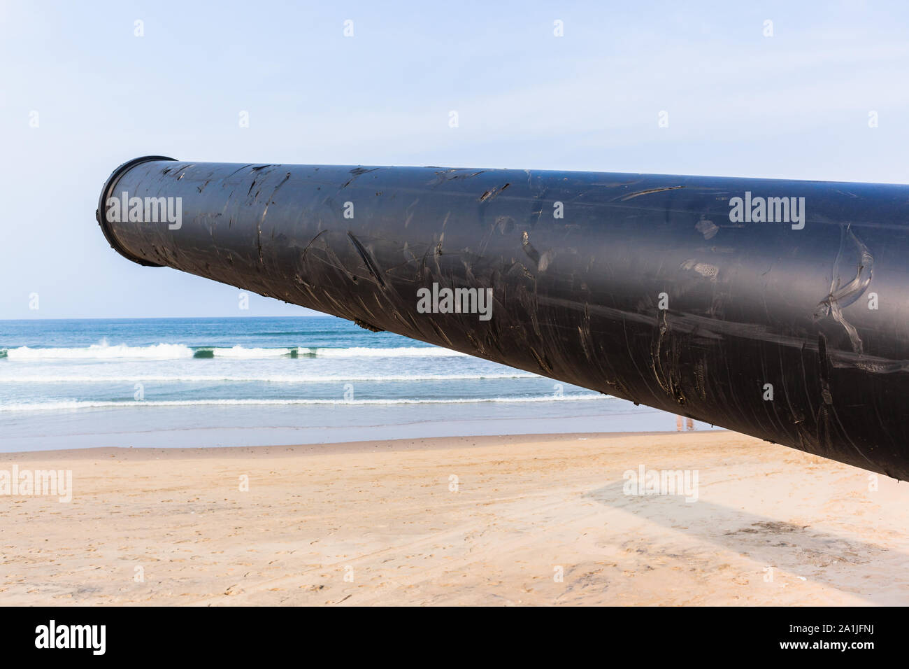Long black plastic industrial pipe suspended in air above sand and ...