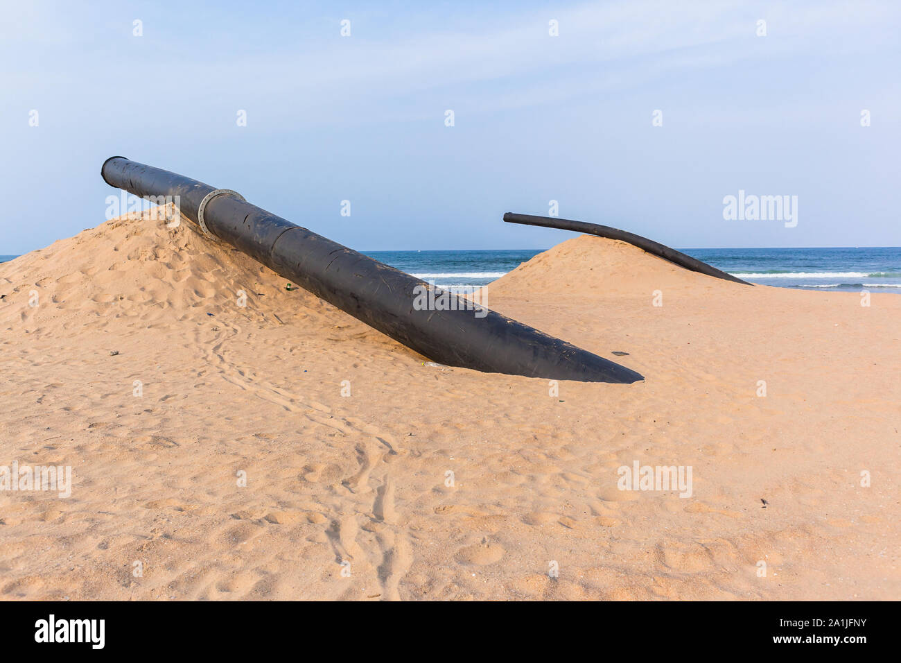Long black plastic industrial pipe suspended in air above sand and ...