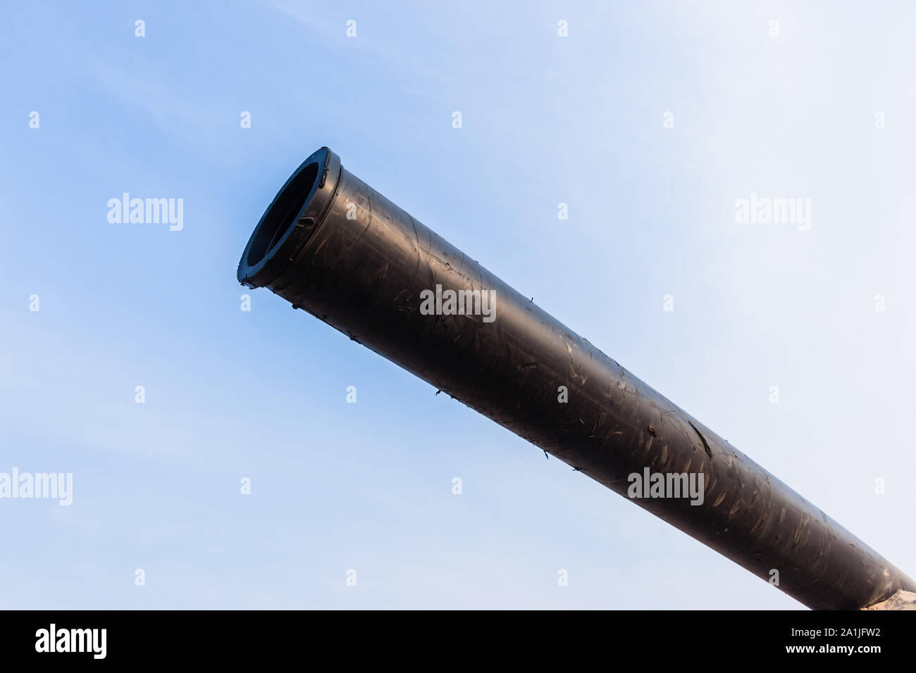 Long black plastic industrial pipe suspended in air above sand and ...