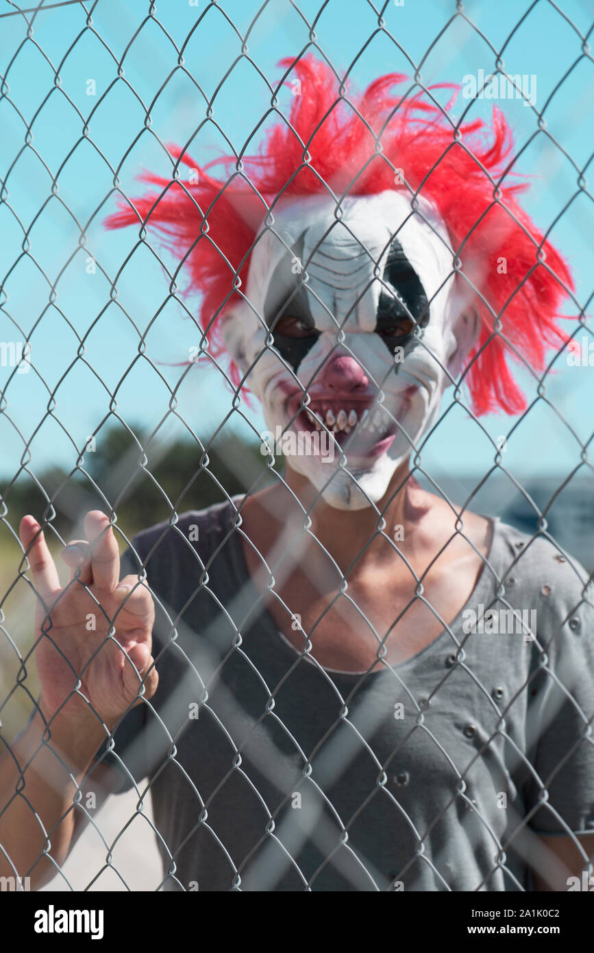 a scary evil clown looking with a threatening look through the wires of ...