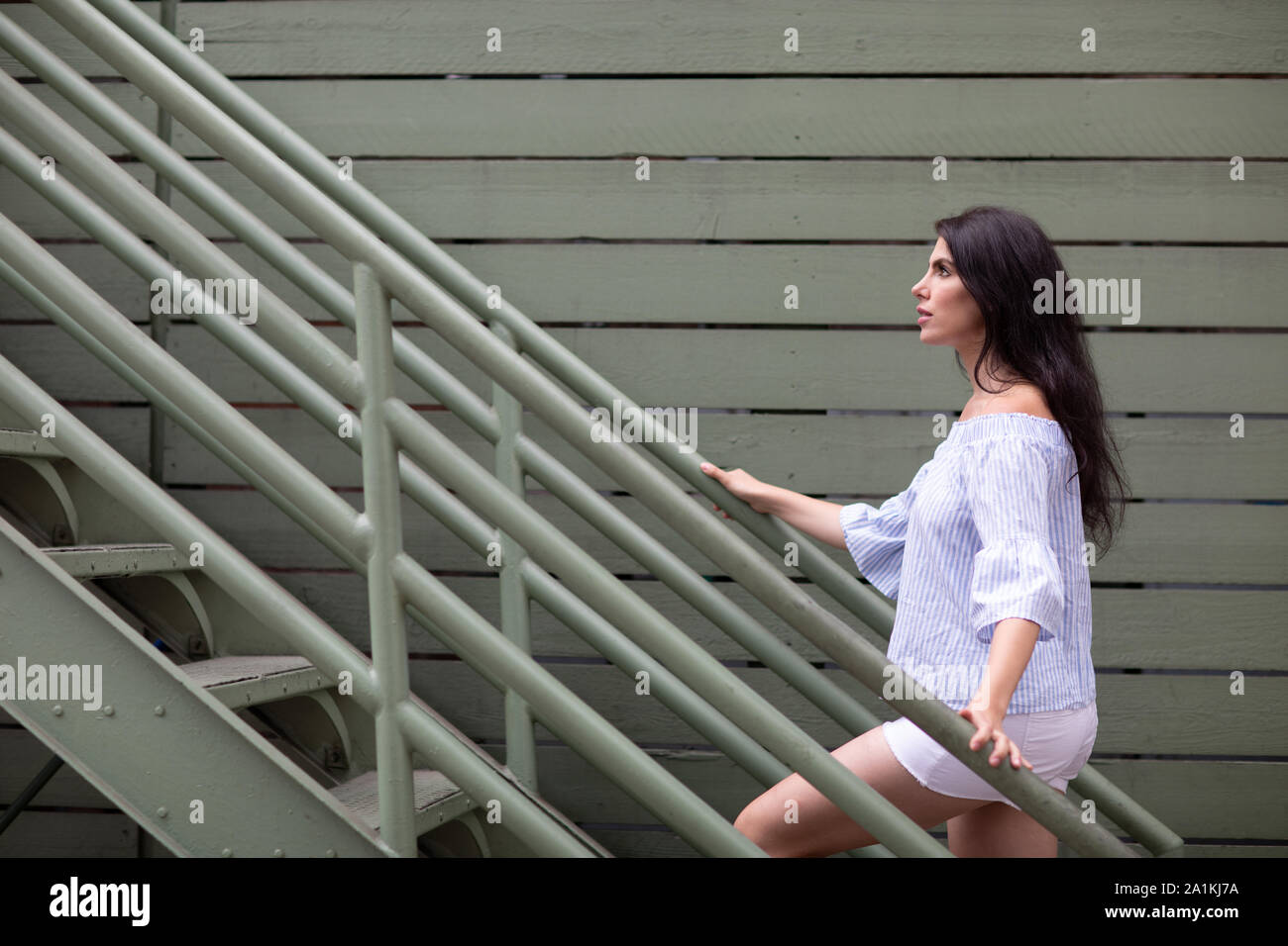 Beautiful young woman climbing industrial stairs on the backstreet ...
