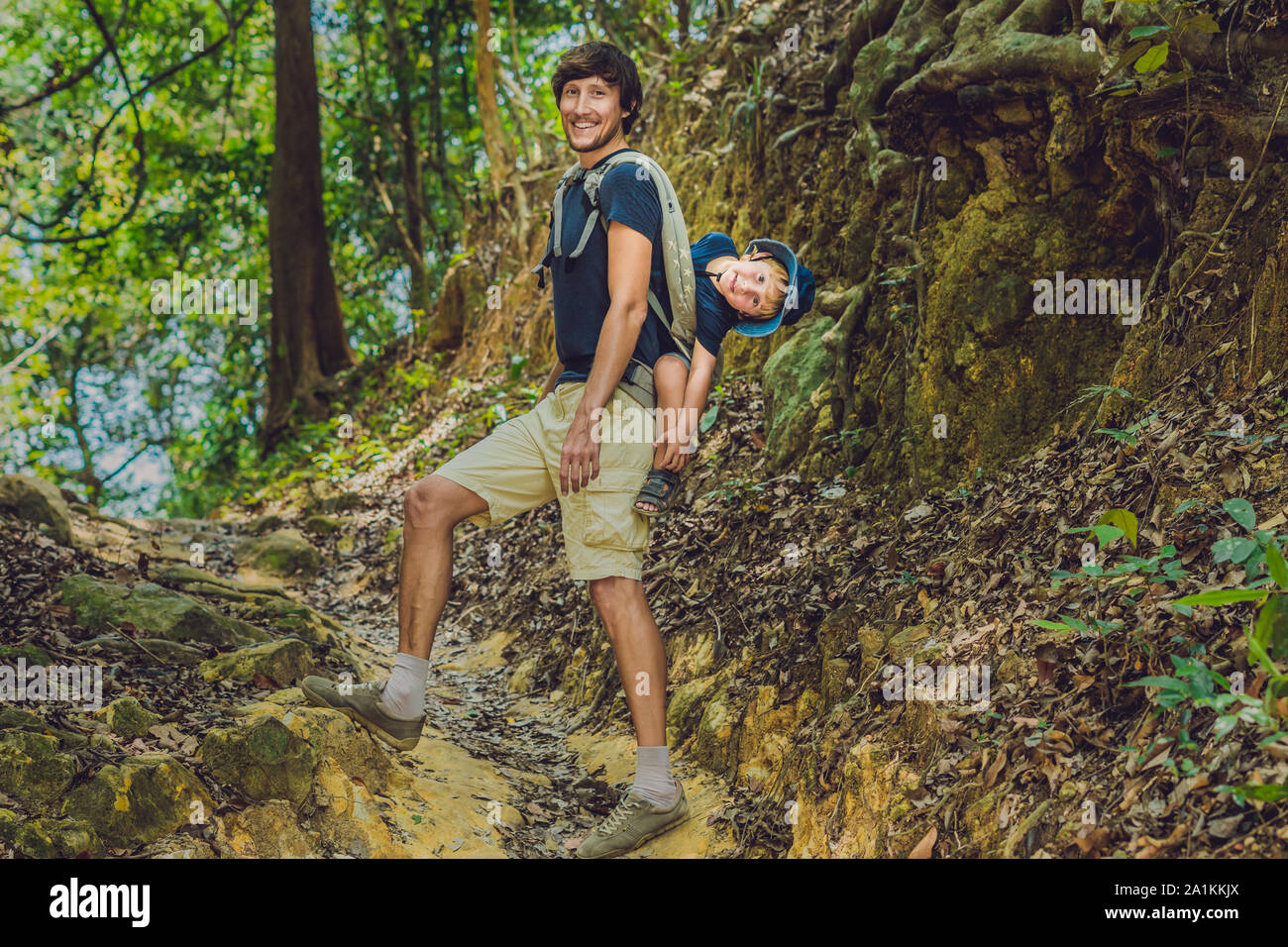 The father carries his son in a baby carrying is hiking in the forest ...