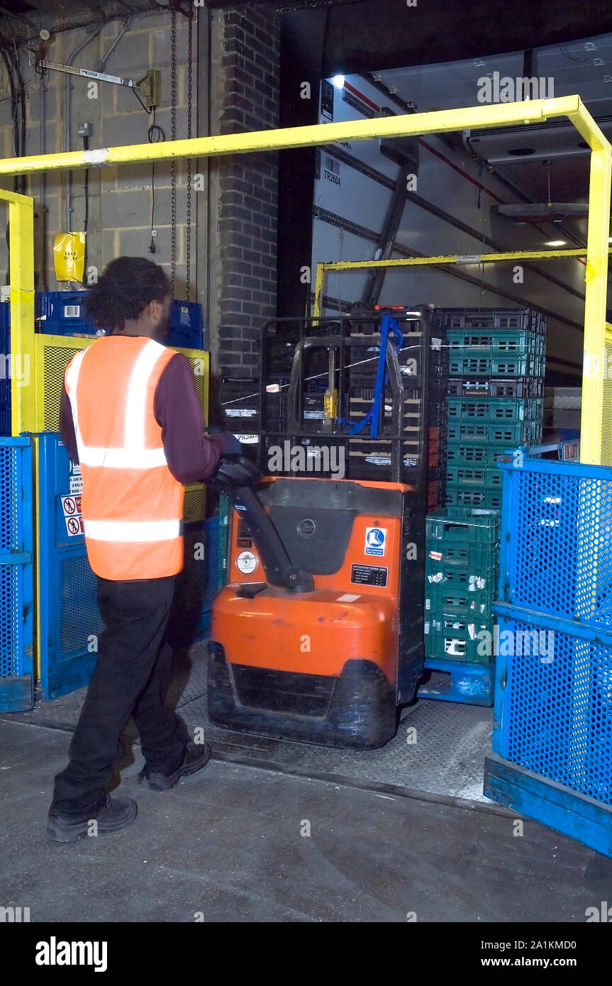 A warehouse worker moving plastic delivery crates using an electric ...