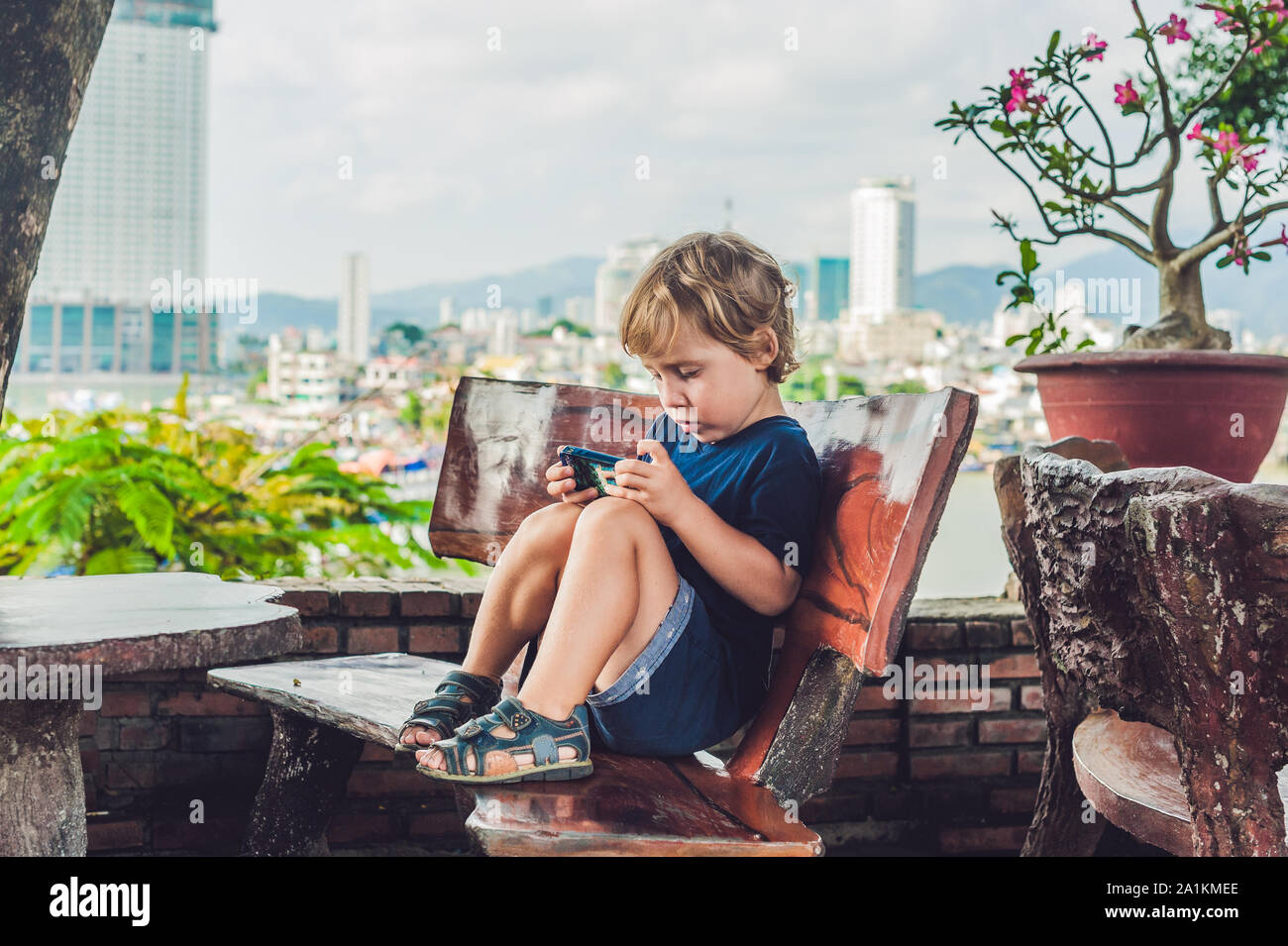 Adorable toddler boy sitting on the bench and playing with smartphone ...