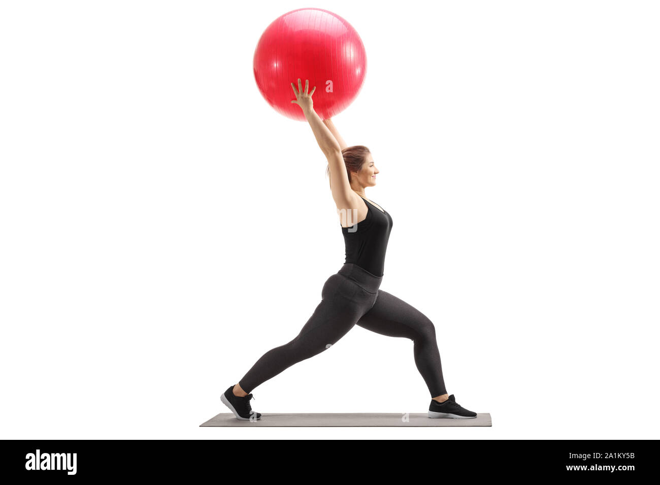 Full length profile shot of a young woman lifting a fitness ball up ...