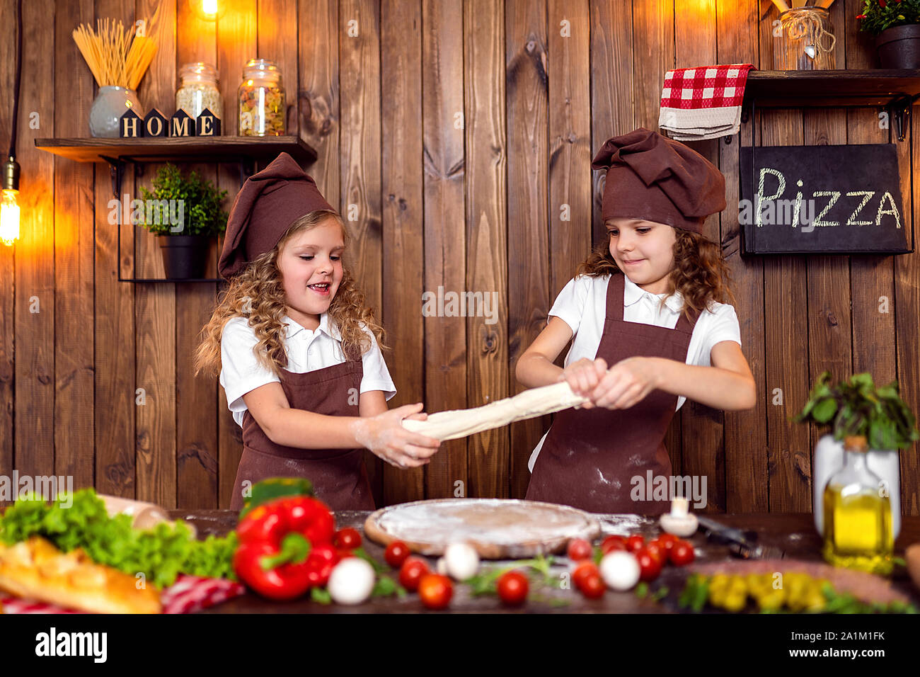 Happy little girls with rolling pin and spatula smiling and looking at ...