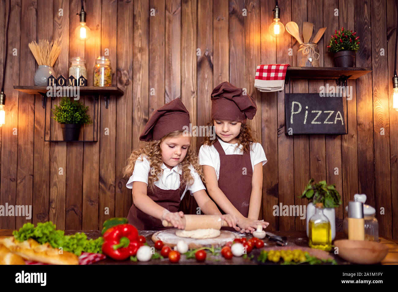 Happy little girls with rolling pin and spatula smiling and looking at ...