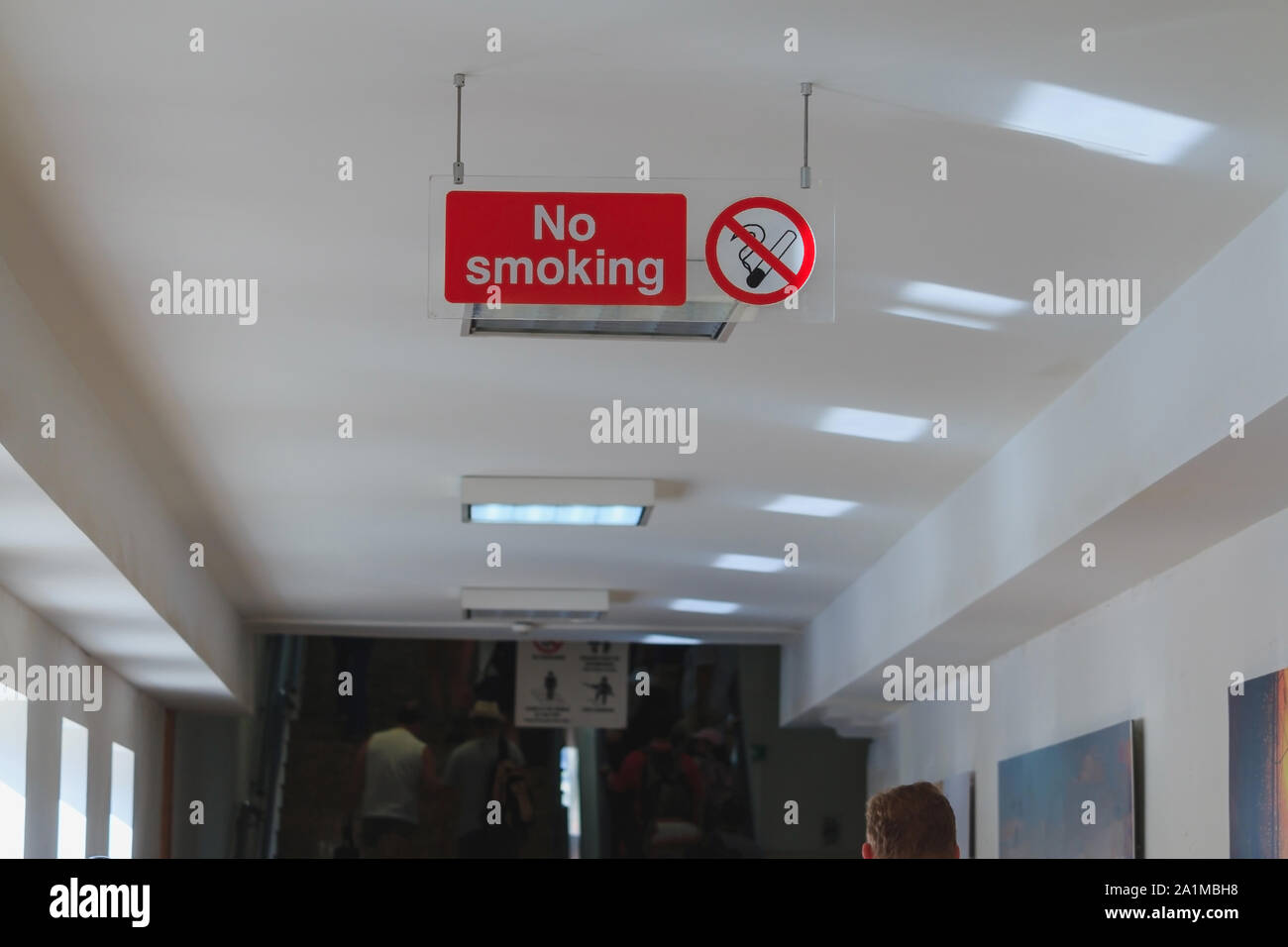 Acrylic no smoking sign attached on ceiling. People walking in corridor ...