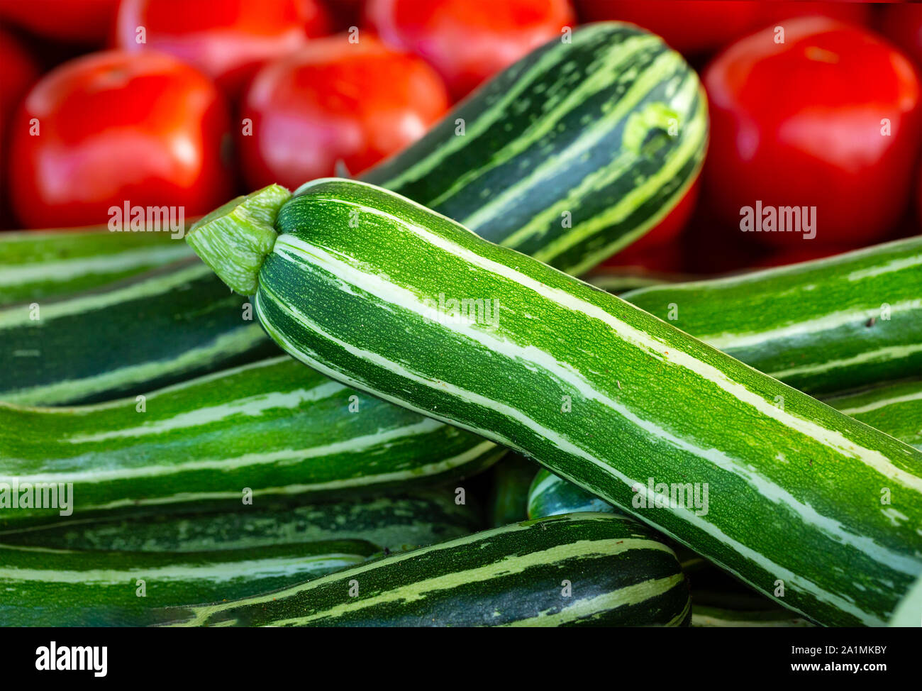 Green striped courgettes with ripe tomatoes in the background Stock ...