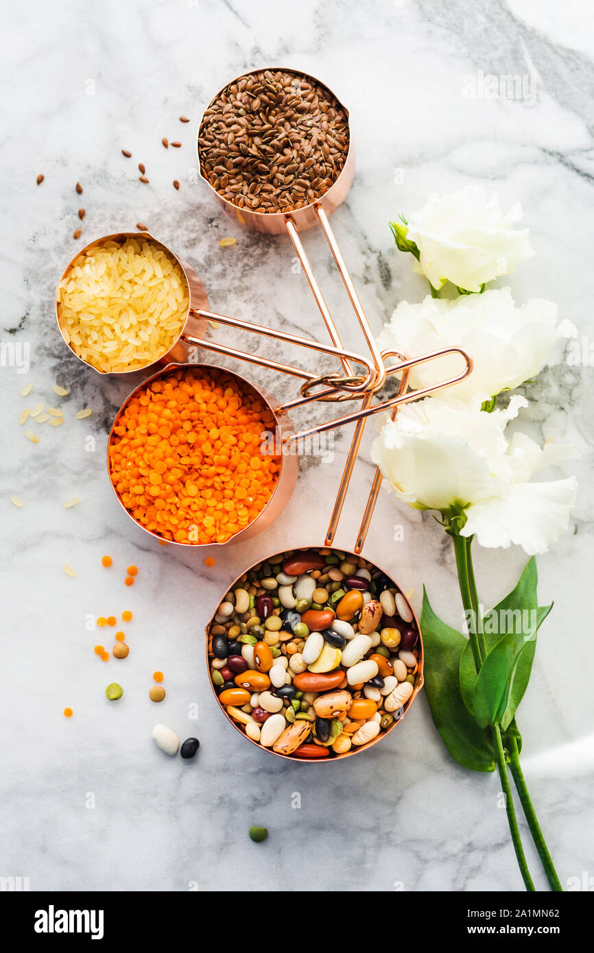 Copper measuring cups on marble table with beans and cereals in the ...