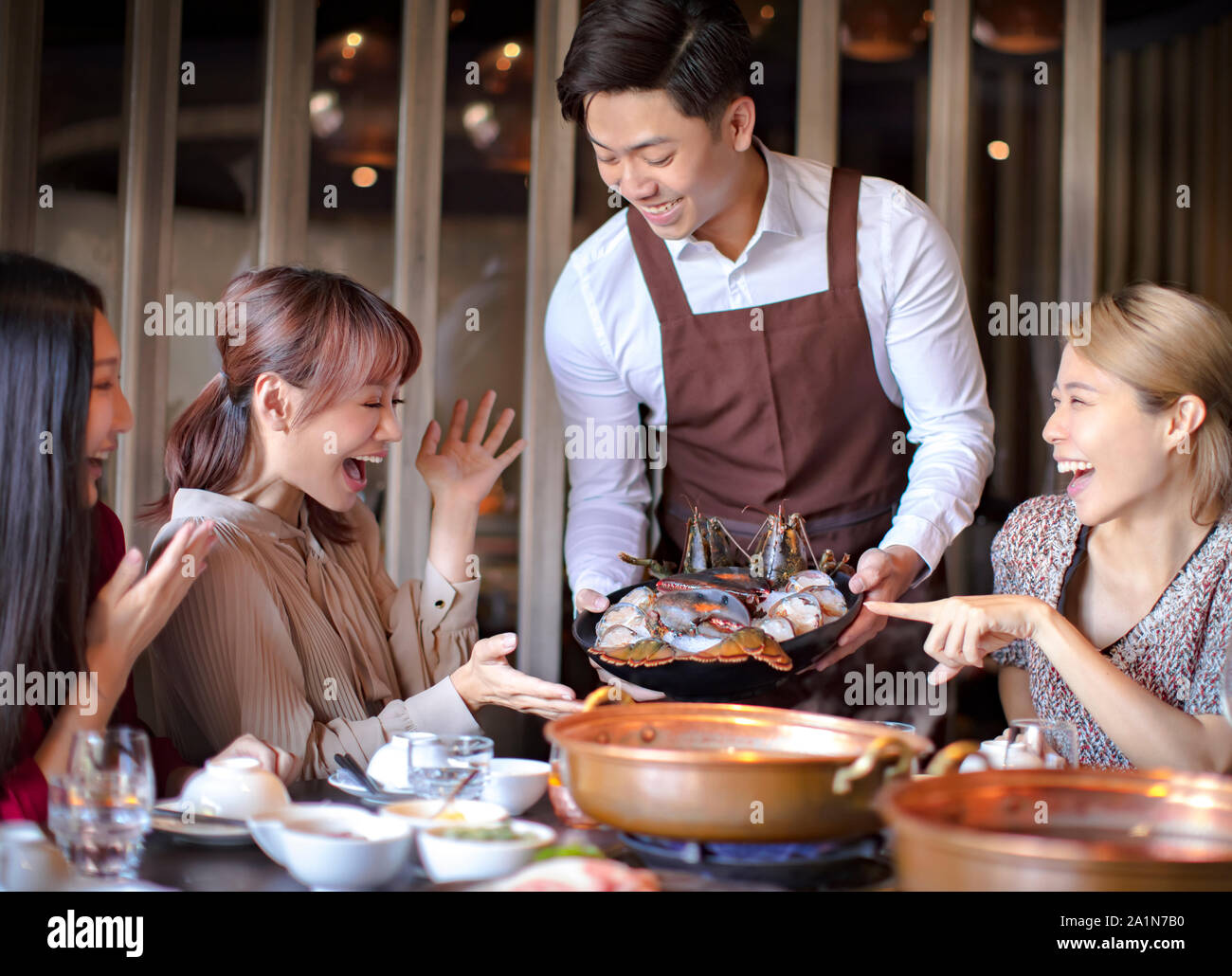 Happy waiter bring seafood and serving group of friends in restaurant ...