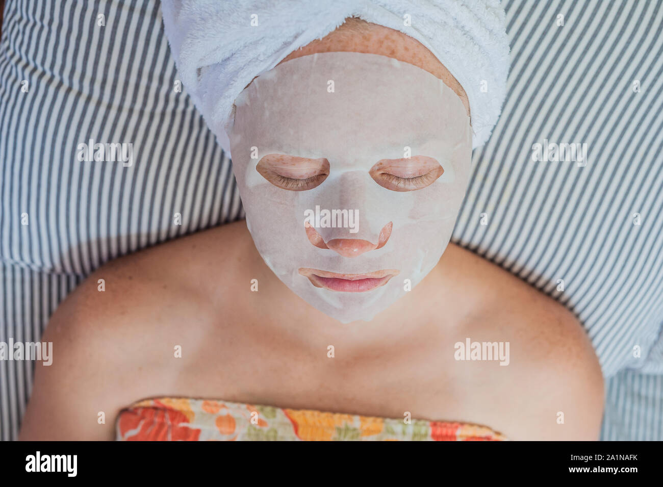 Young red-haired woman relaxing on a bed. Sheet mask on her face Stock ...