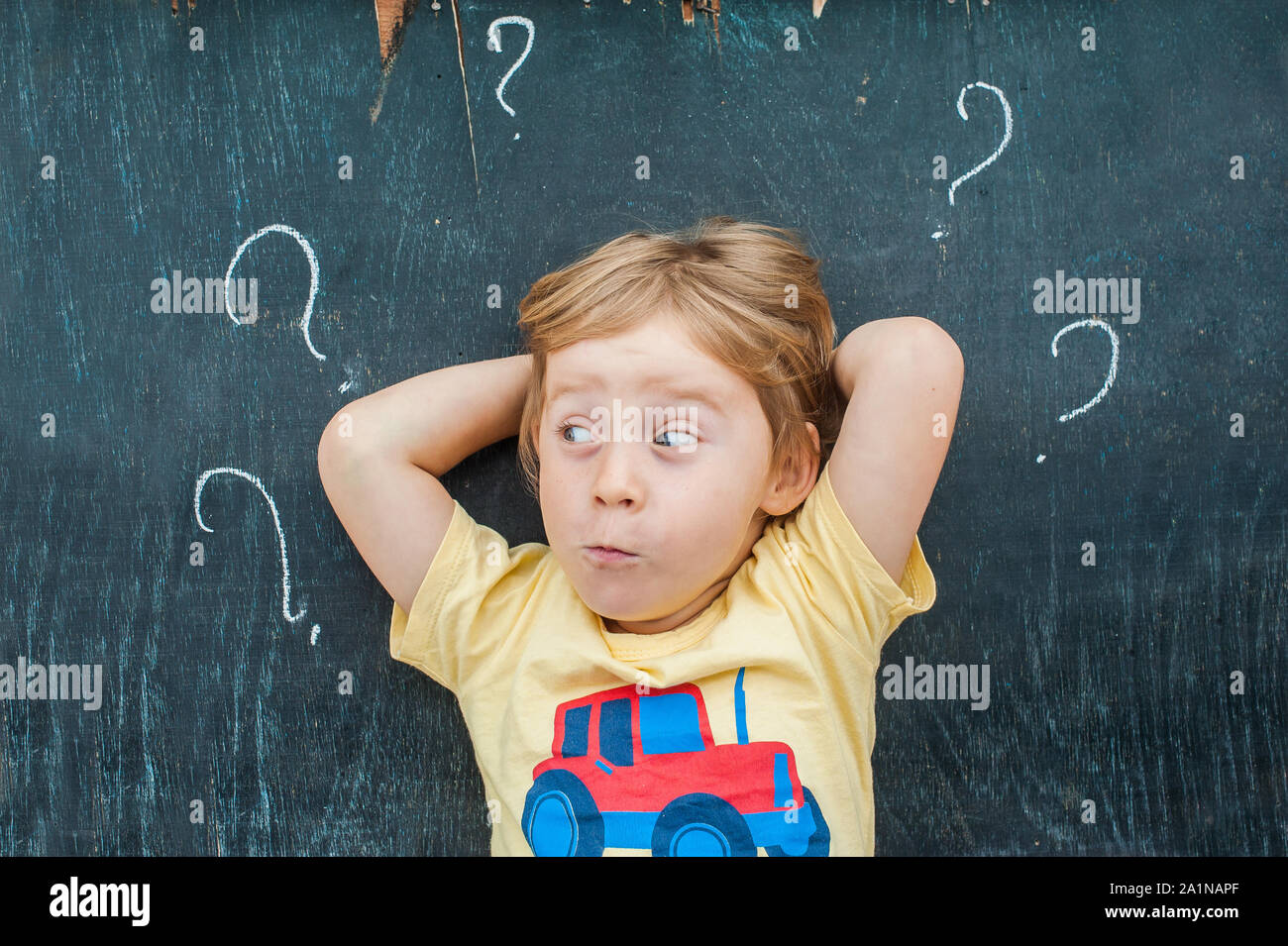 Top view of a little blond kid boy with question mark on blackboard ...