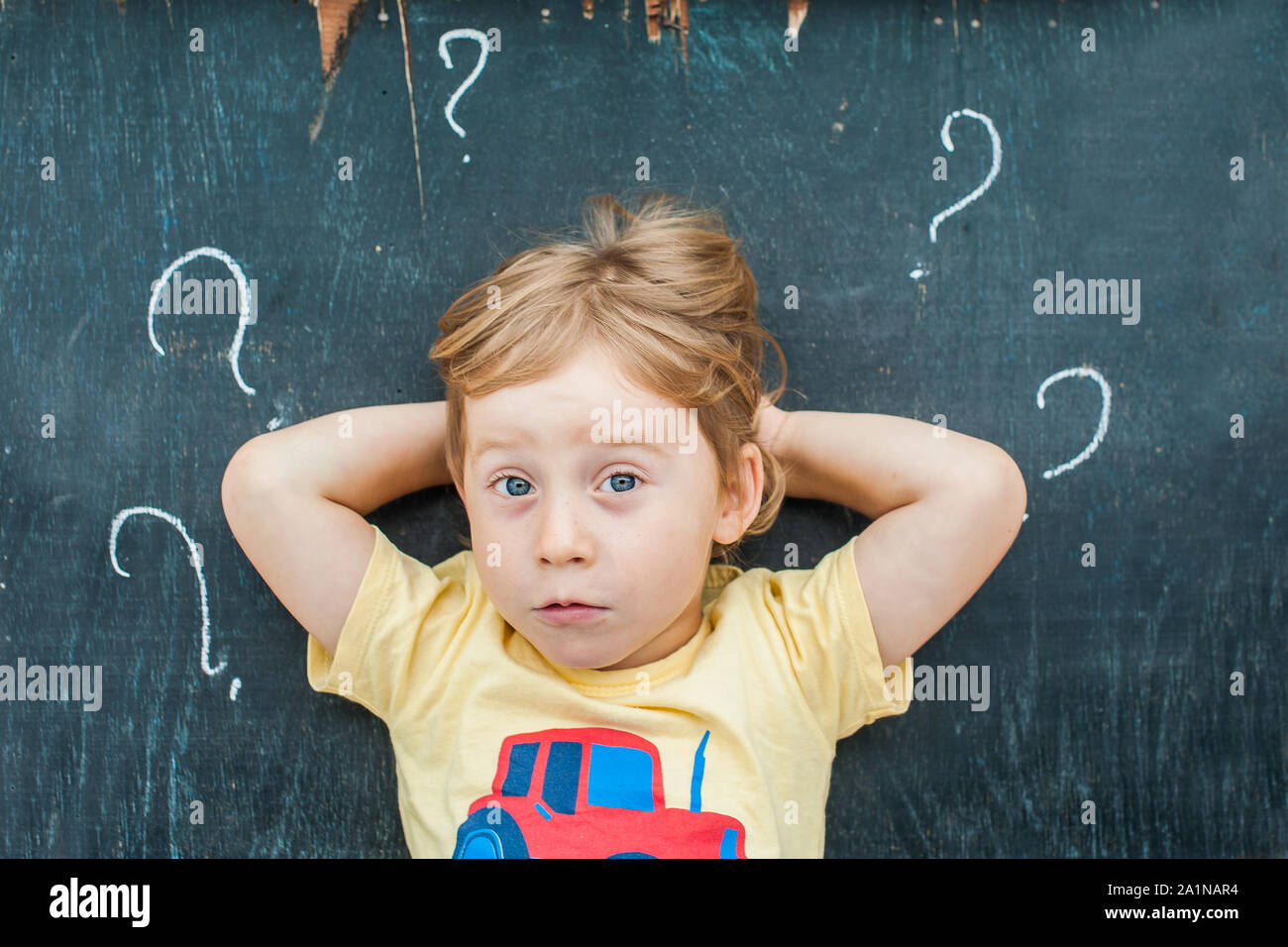 Top view of a little blond kid boy with question mark on blackboard ...