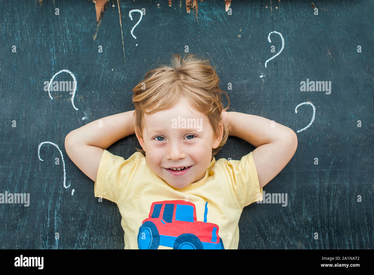 Top view of a little blond kid boy with question mark on blackboard ...