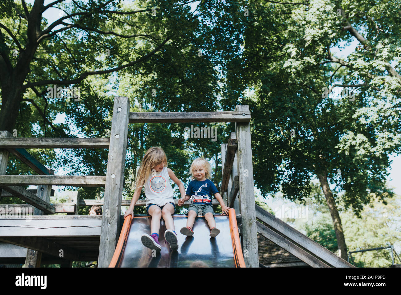 Two young children at the top of a slide on a play structure surrounded ...