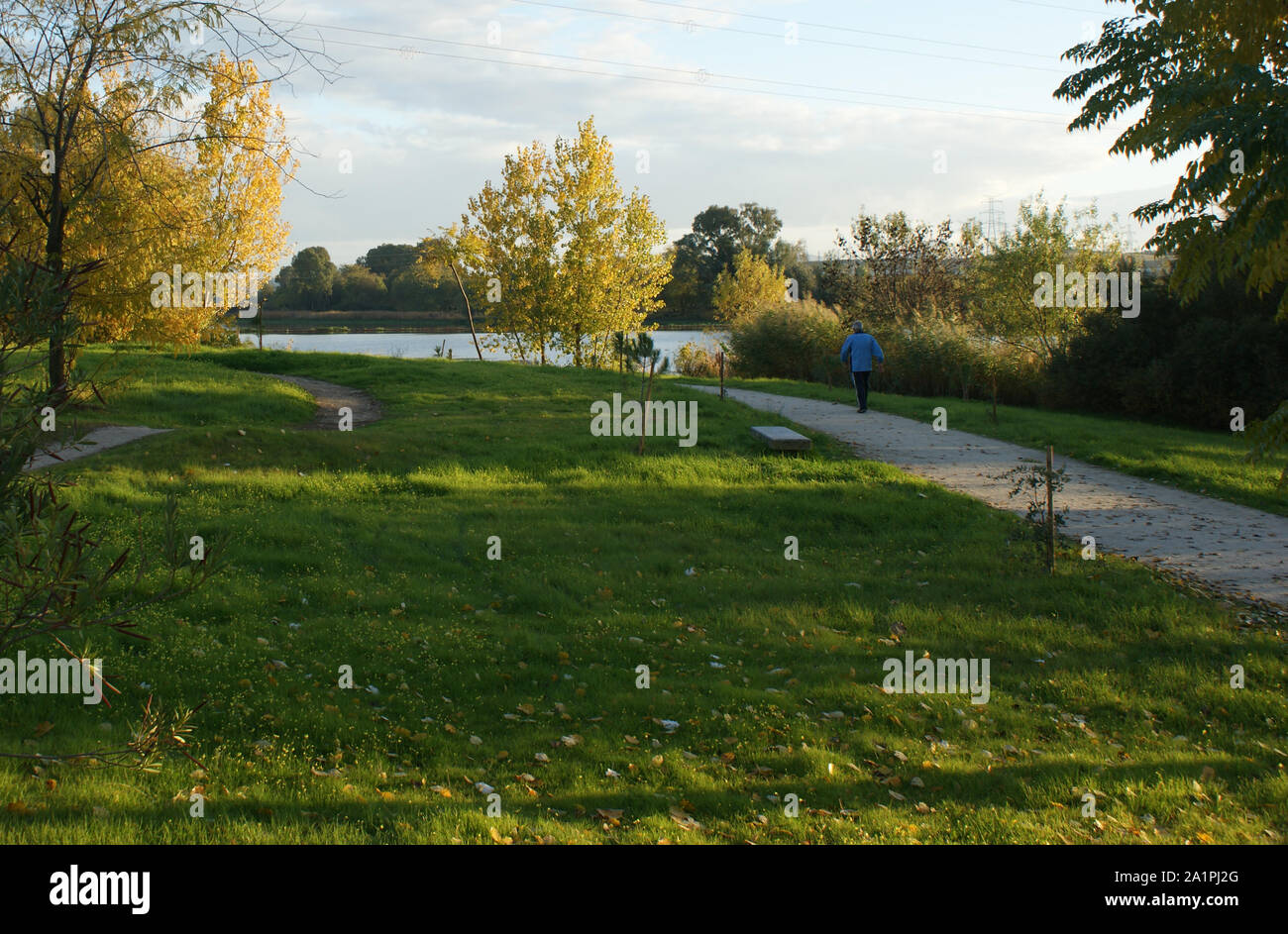 Park with path to the river and man walking on an autumn sunnny day ...