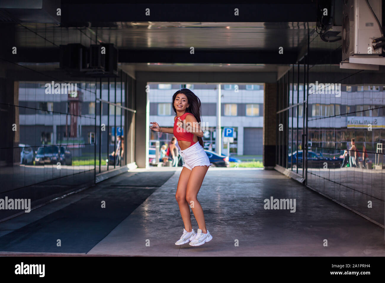 Young beautiful brunette woman jumping in mirror arch of building Stock ...