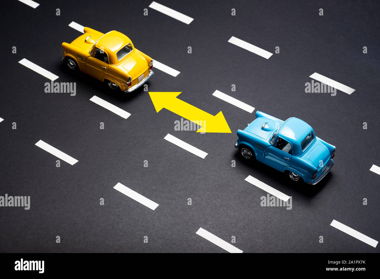 Two toy cars on the road one after another. One is blue one is yellow ...