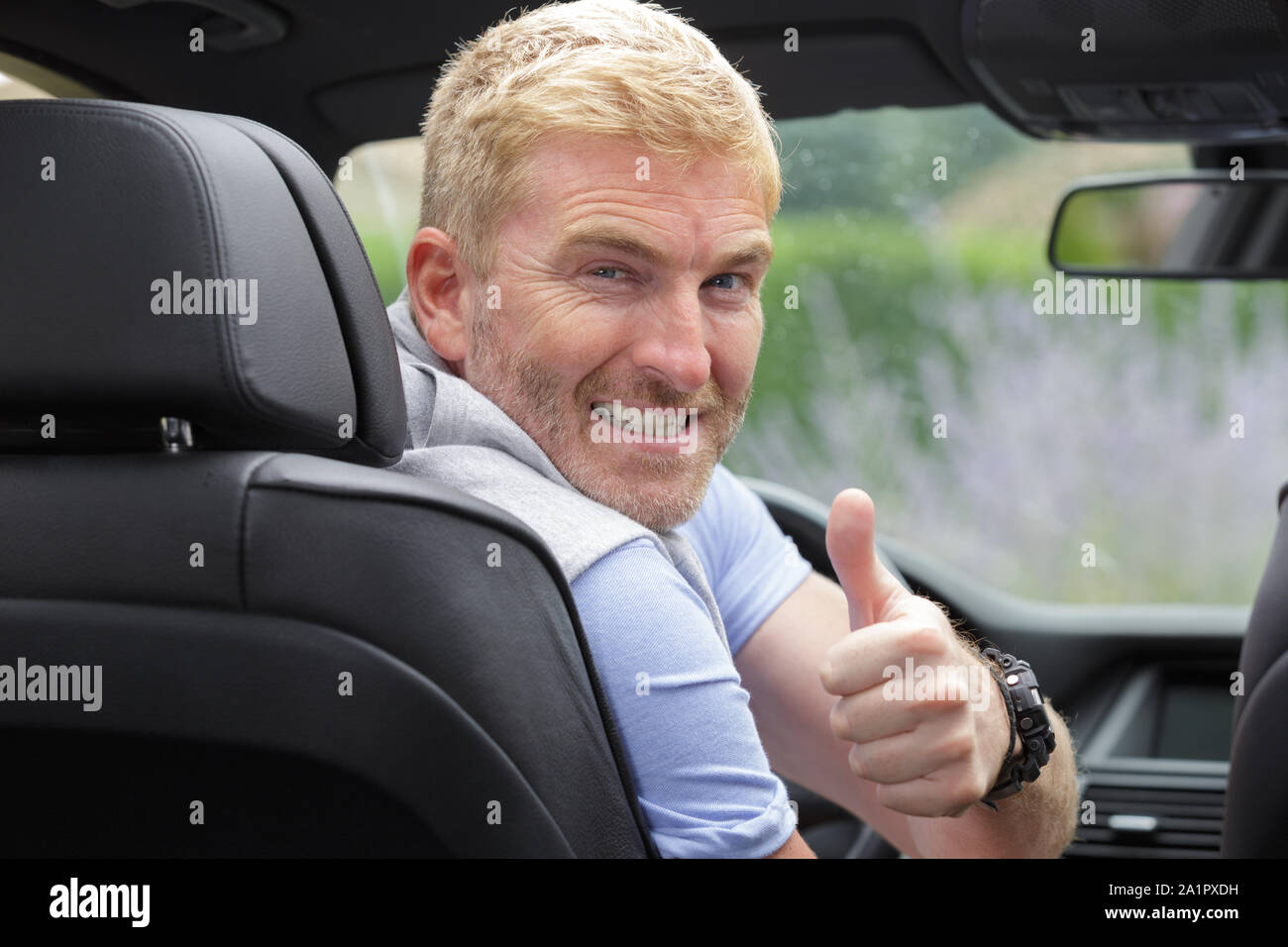 male driver turning to back of car with thumbs up Stock Photo - Alamy