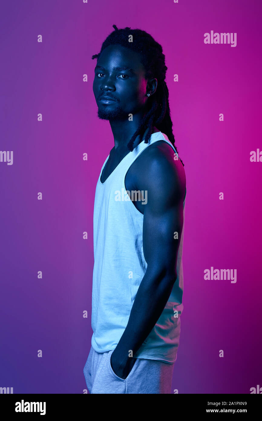 young good looking man with dreadlocks holding palms in his pockets ...