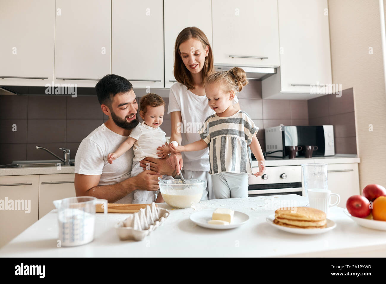 cheerful smiling couple and their kids coking tasty cake, rejoicing at ...