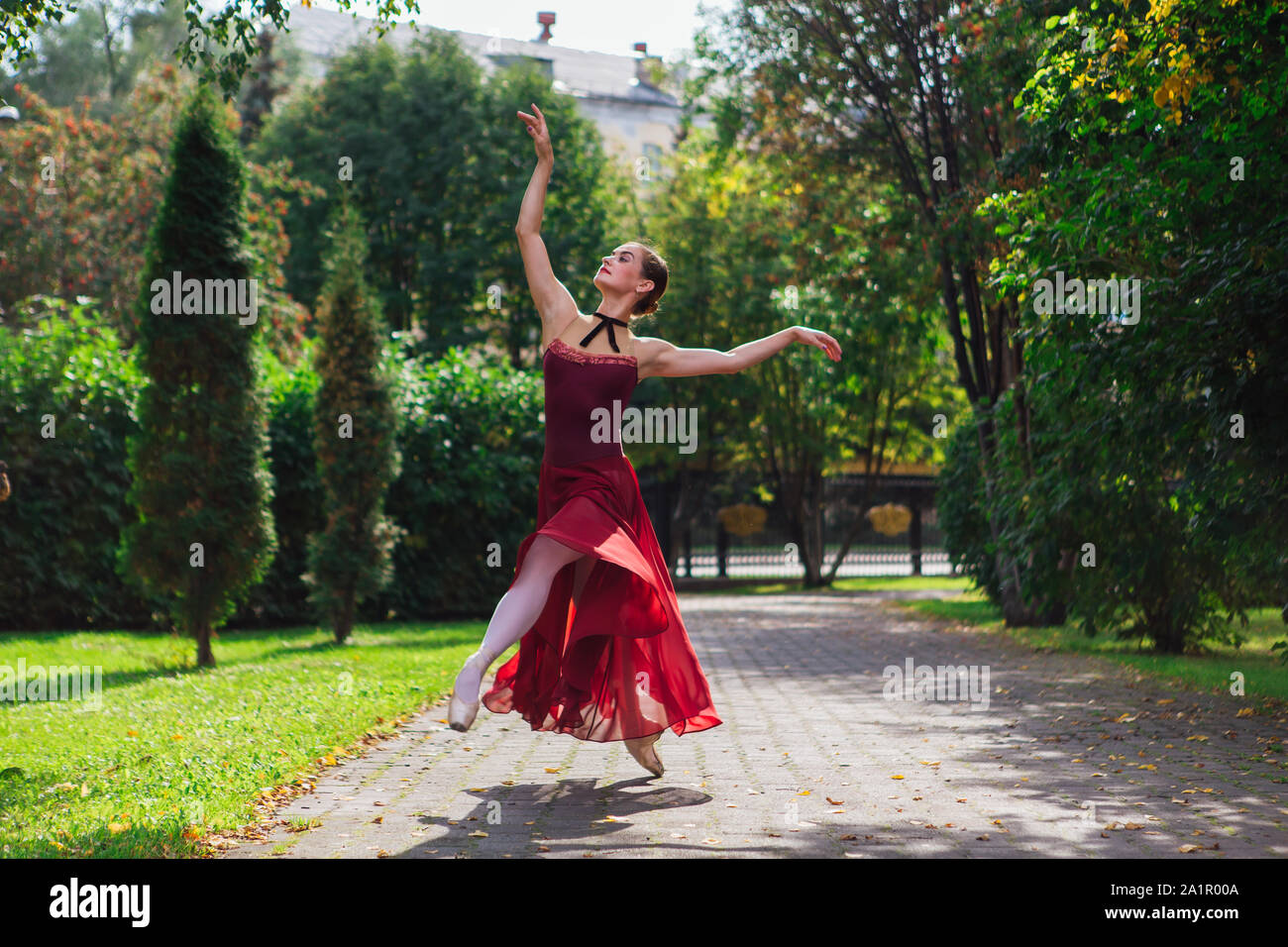 Woman ballerina in red ballet dress dancing in pointe shoes in autumn ...