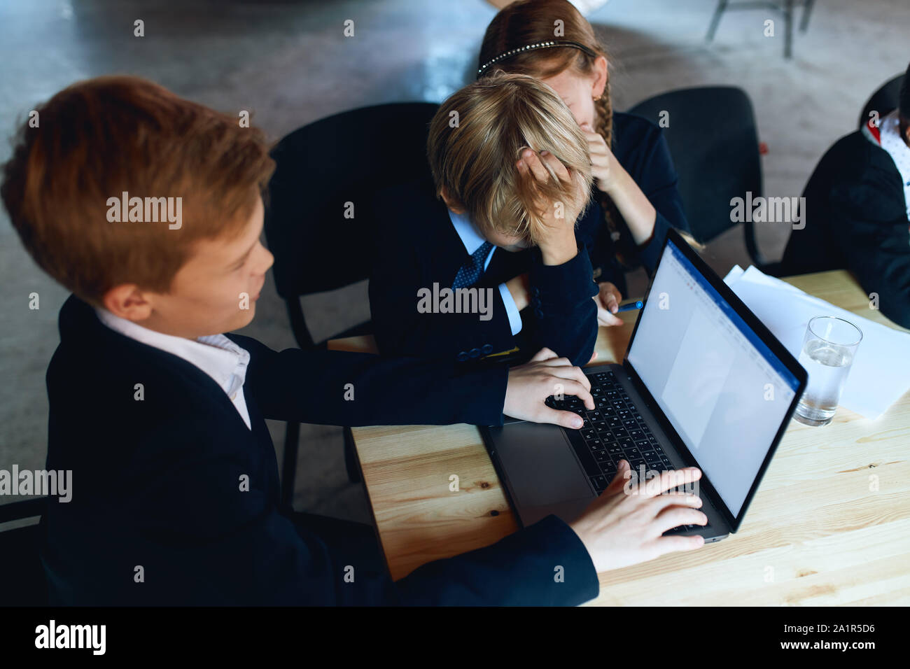 boy typing something on laptop while his friends are laughing at him ...