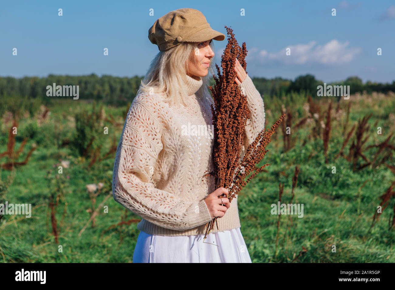 Happy beautiful blond woman dressed in a cap, sweater and white long ...