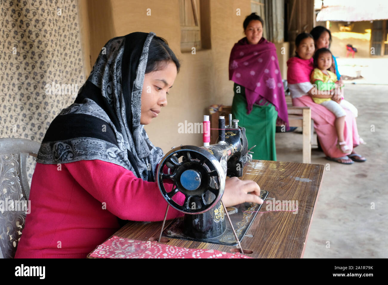 Woman is tailoring with her sewing machine in front of her house ...
