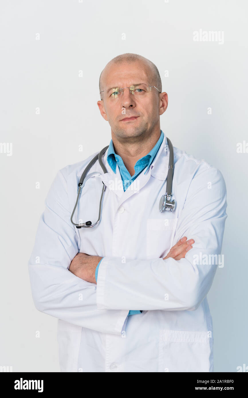 Young serious cross-armed doctor in whitecoat standing on white ...