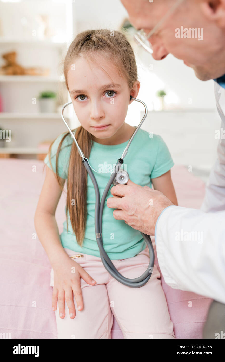 Puzzled little girl listening to her heartbeat while doctor holding ...