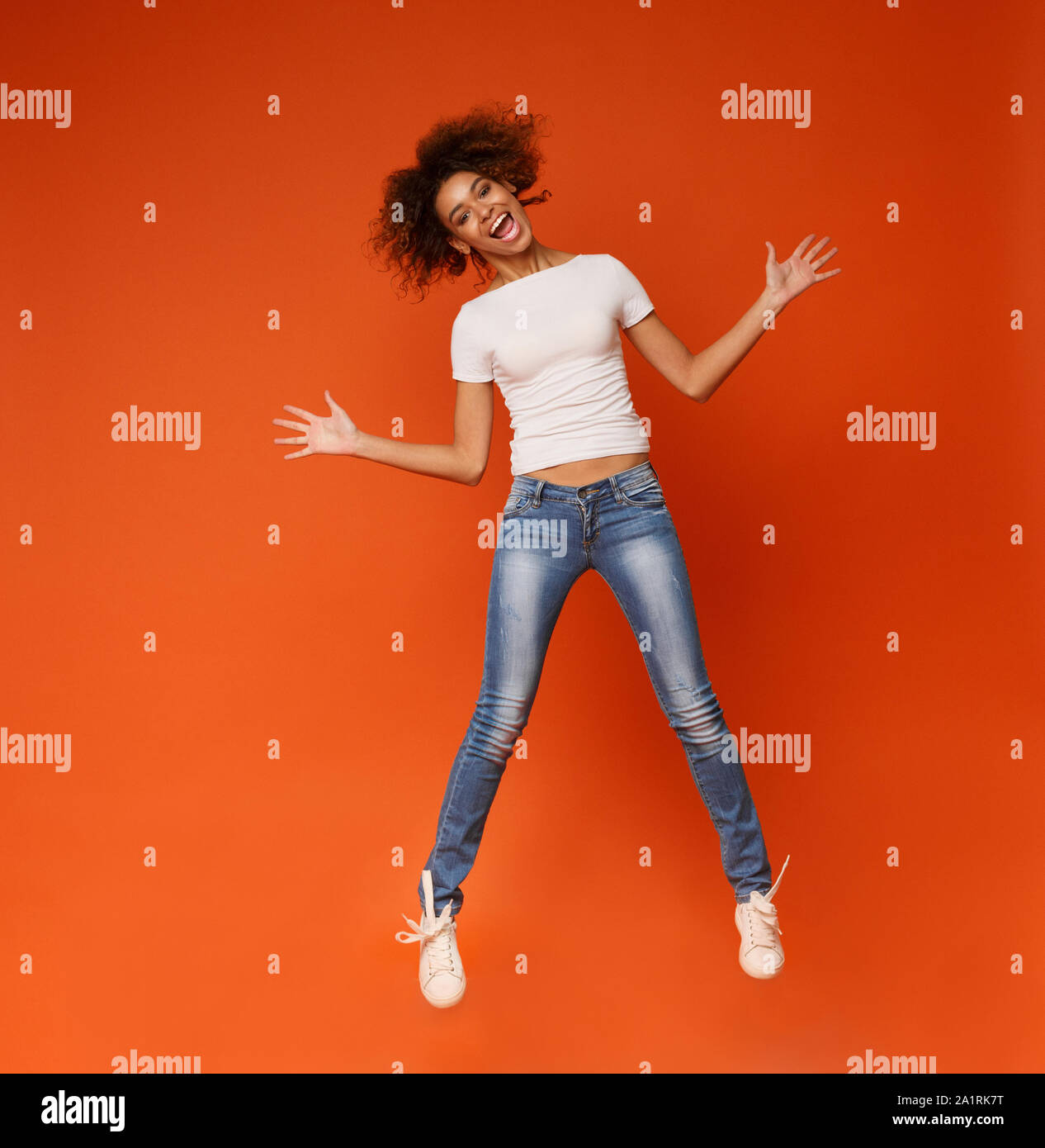 Cheerful african girl jumping in air, orange background Stock Photo - Alamy