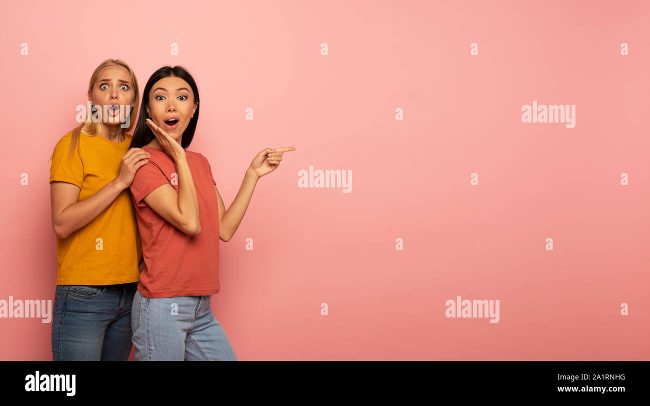 Two girls indicates something. Amazed expression face. Pink background ...