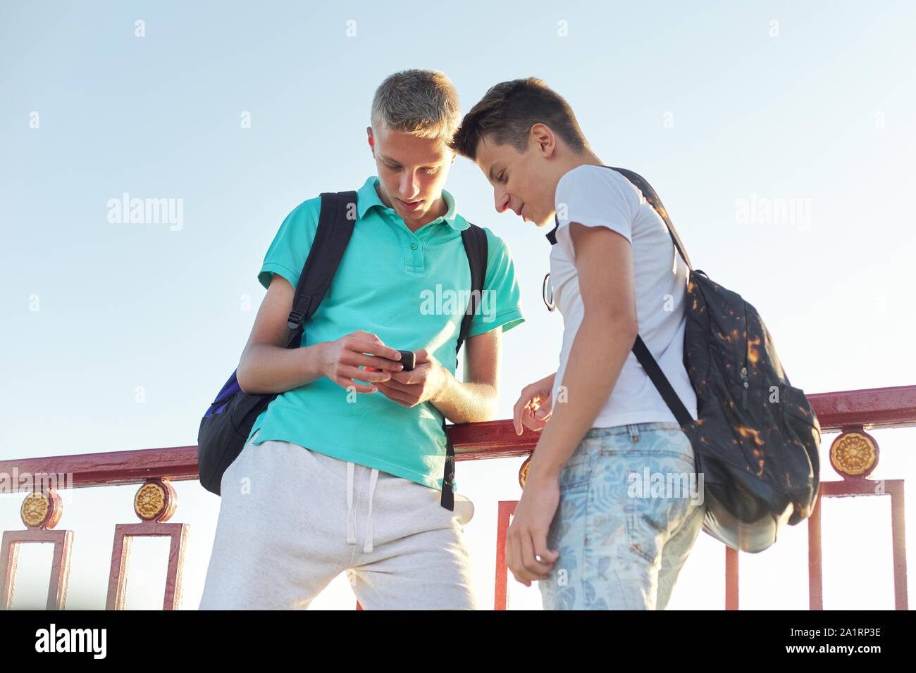 Two friends teenage boys using smartphone, talking and smiling, outdoor ...