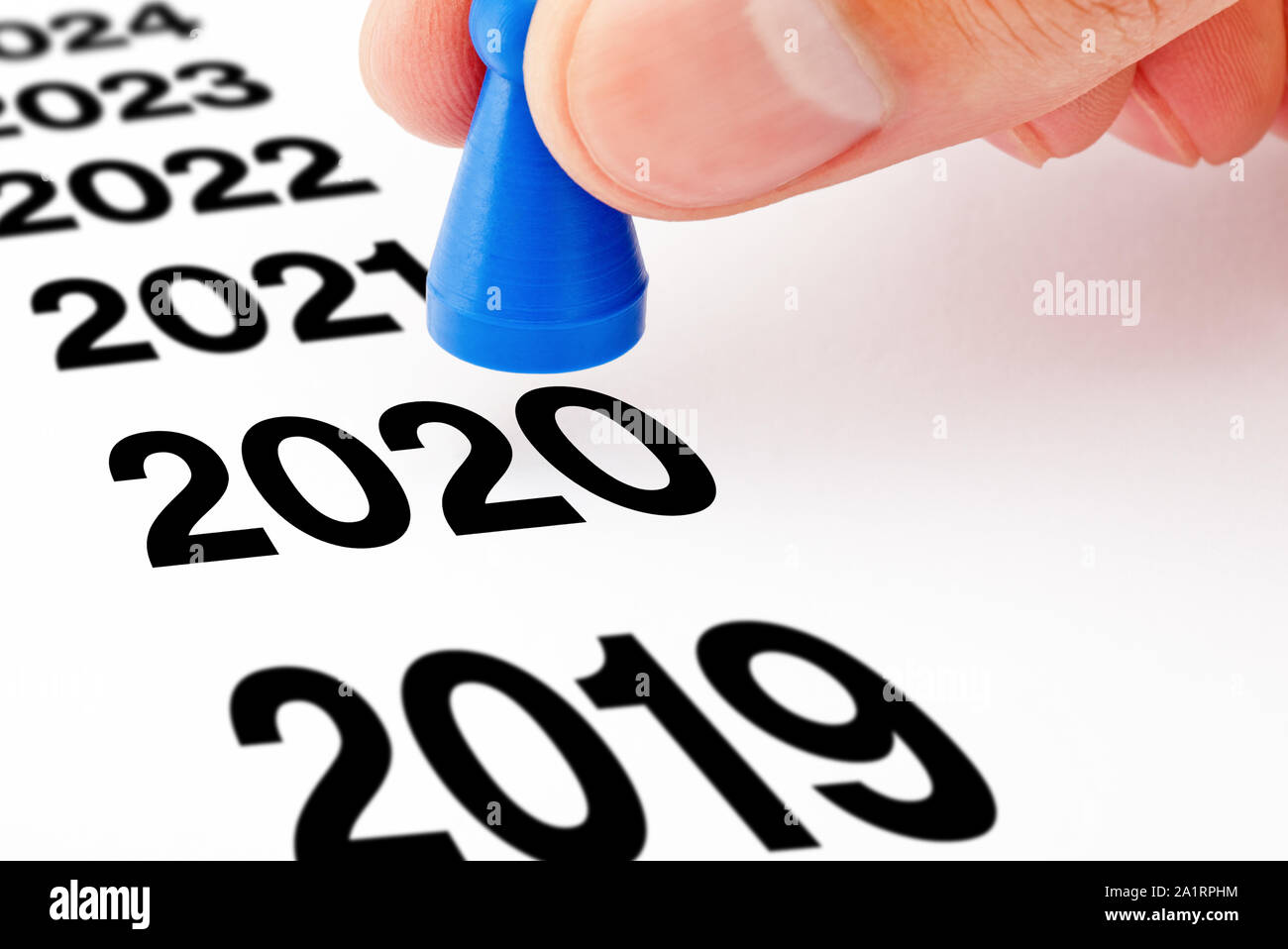 Hand moving a blue pawn from year 2019 to year 2020 printed on white ...