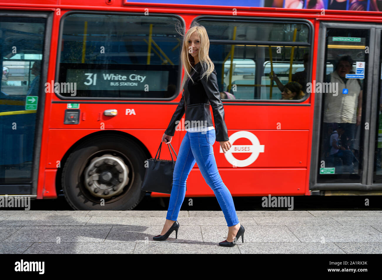 Attractive young urban girl at the bus stop to catch a red double ...