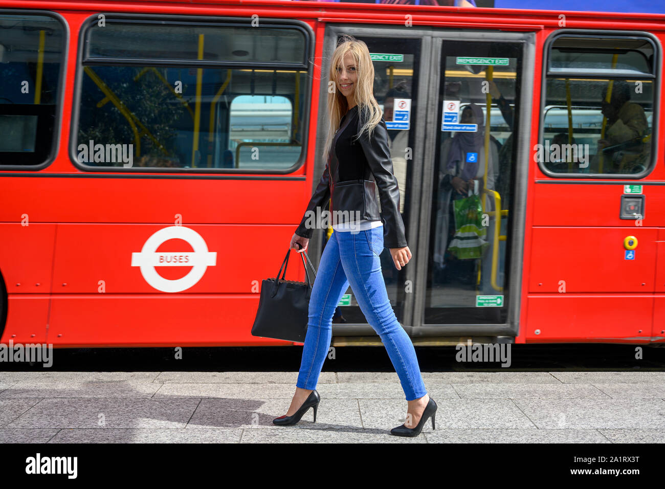 Attractive young urban girl at the bus stop to catch a red double ...