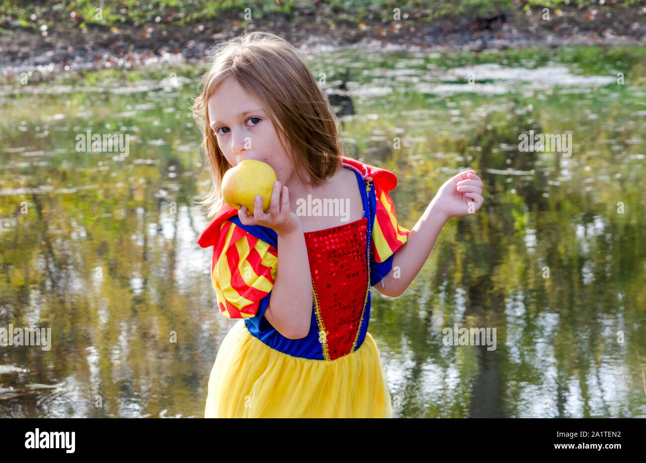 A young girl enjoys a fresh apple, as she plays dress up in her ...
