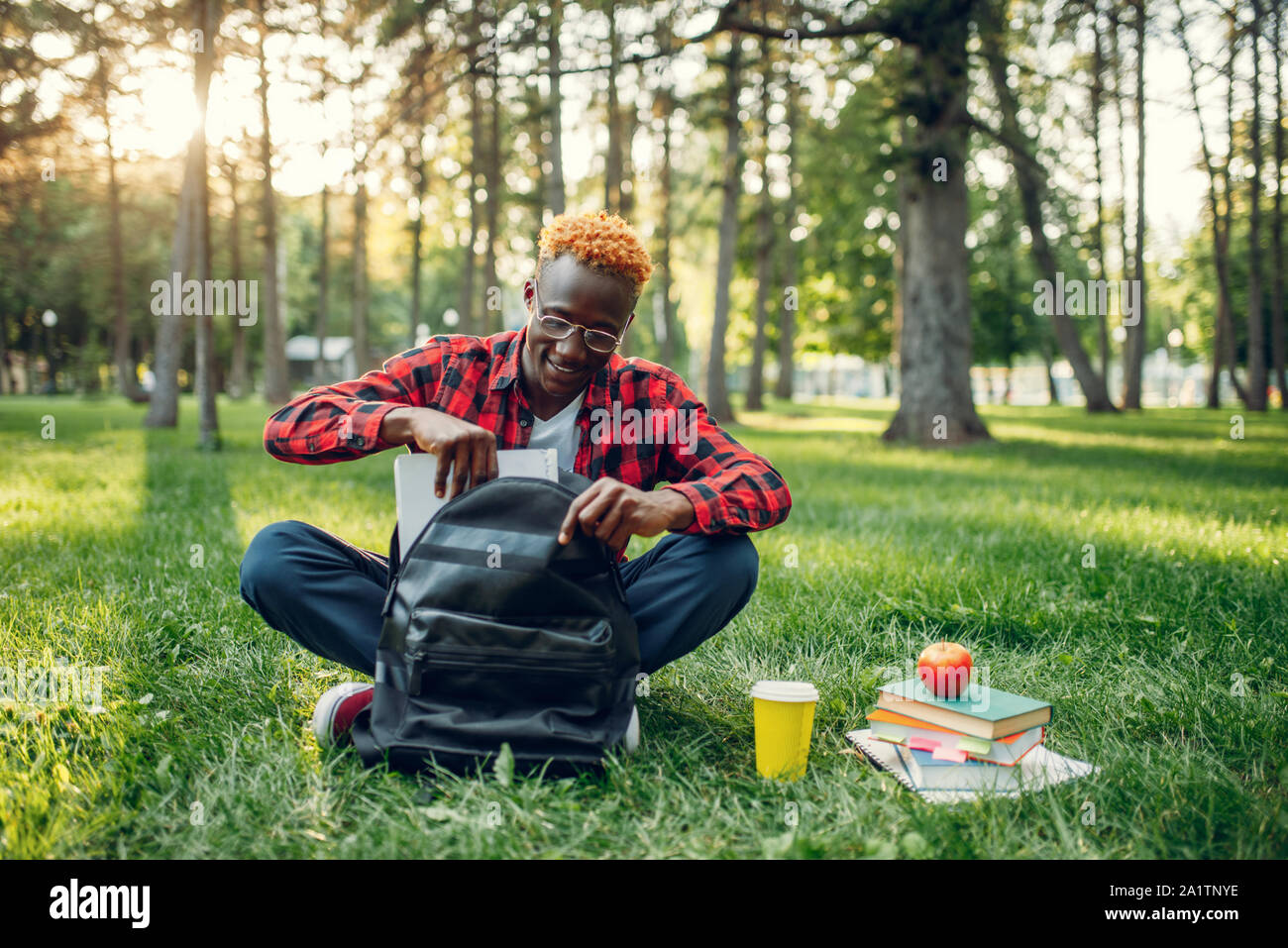 Black student with backpack sitting on the grass Stock Photo - Alamy