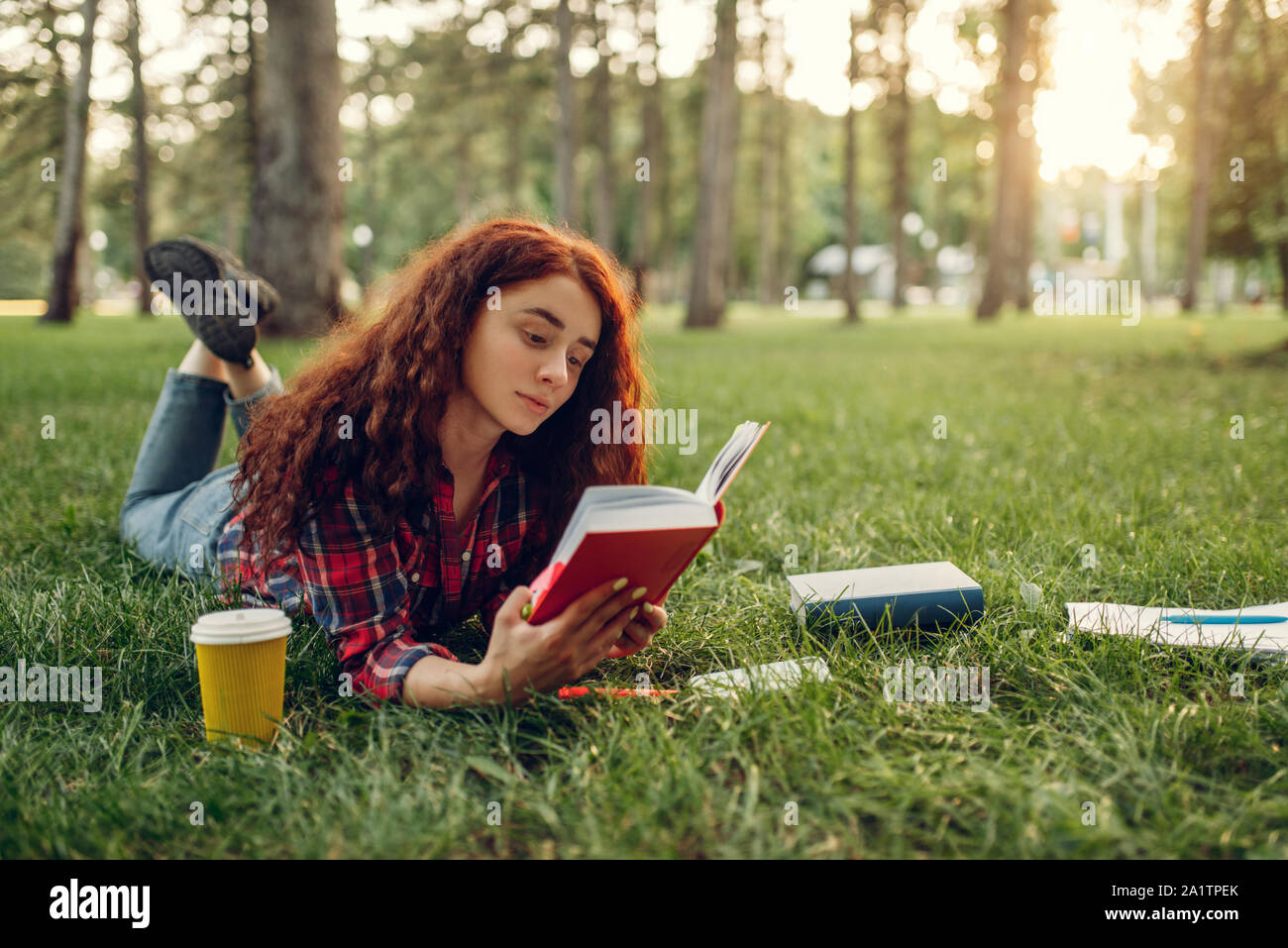 Female student with cup of coffee lying on grass Stock Photo - Alamy