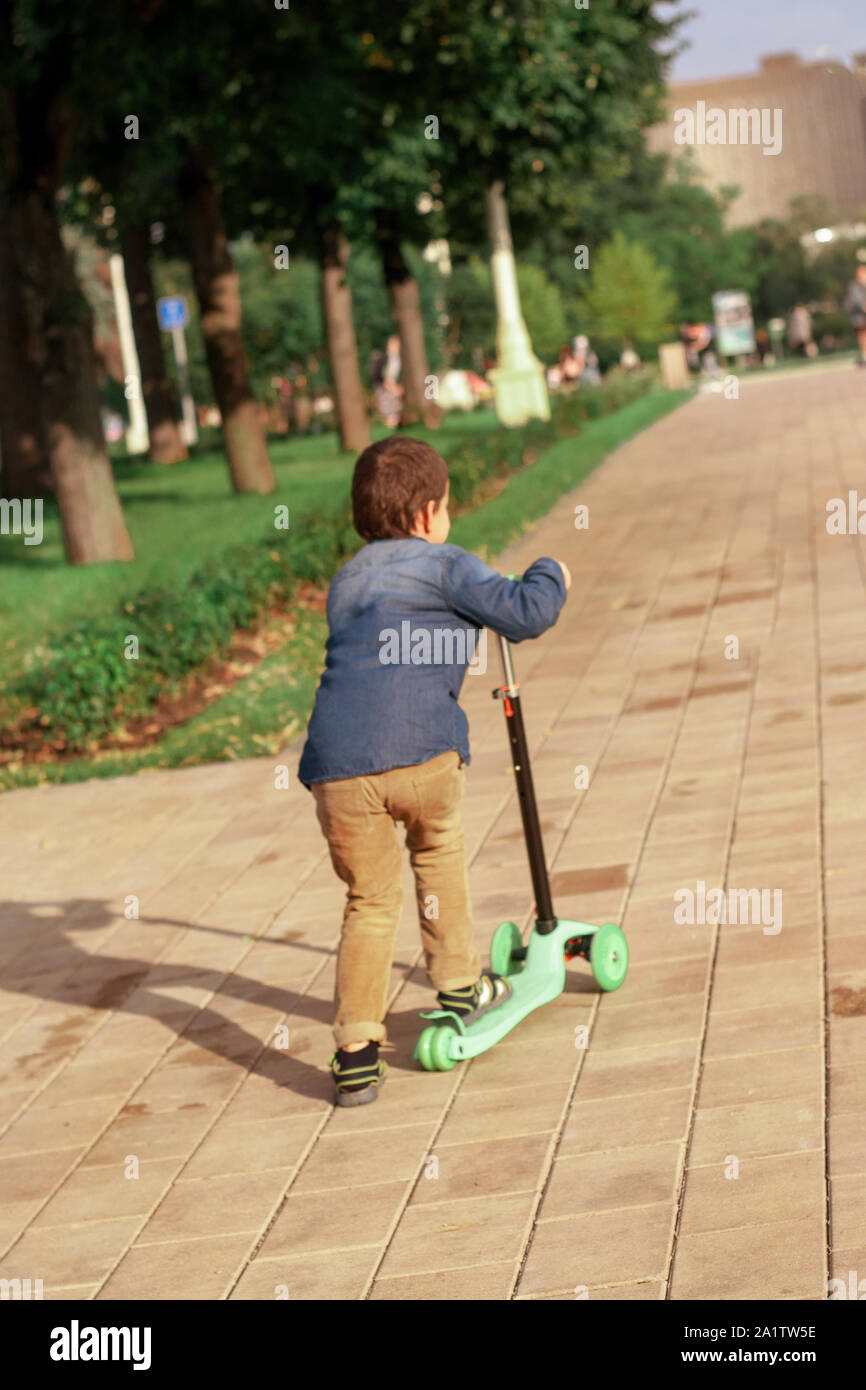 A preschool boy learns to ride a scooter in a park. The first steps in ...