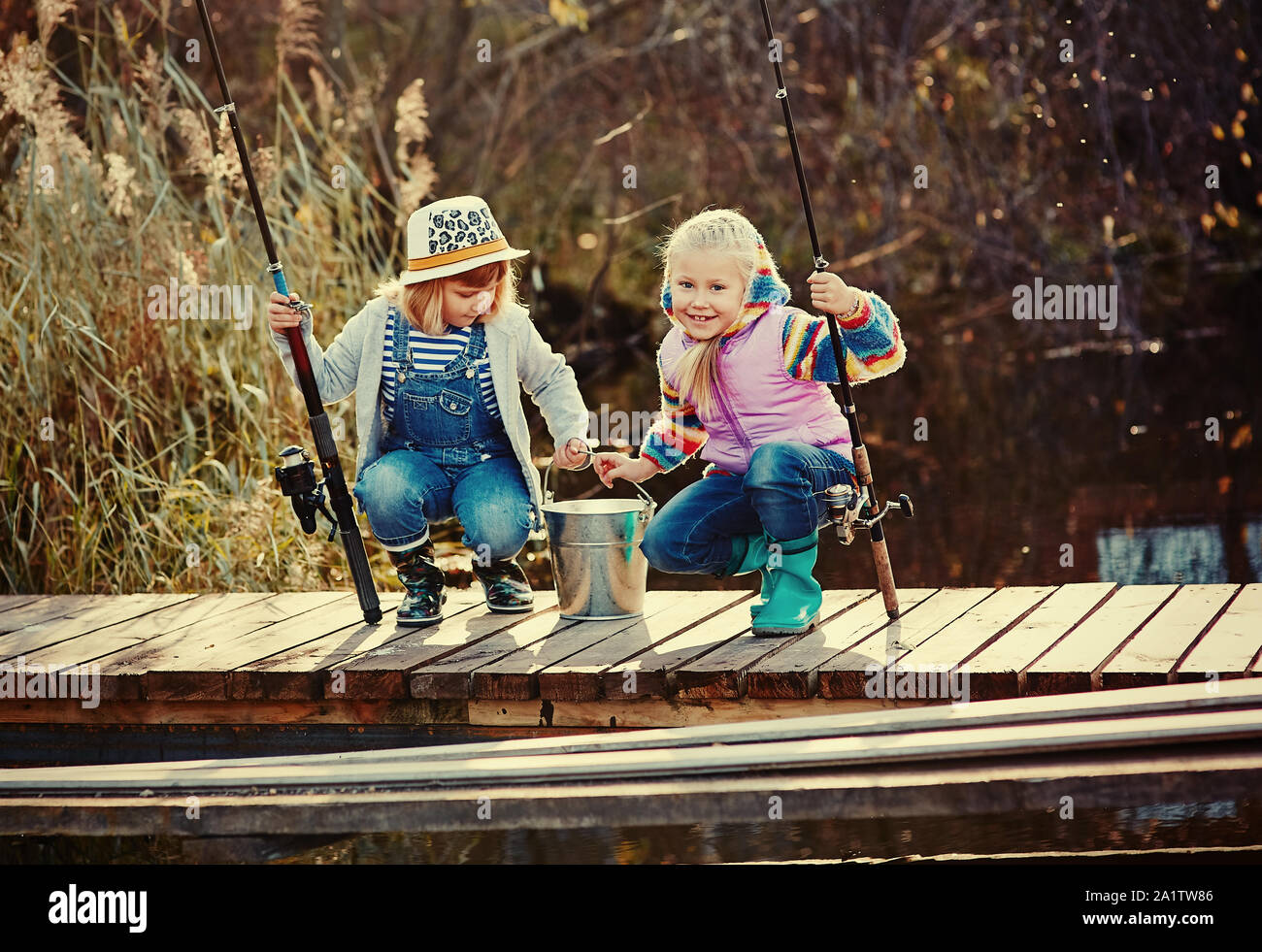 Two little girls with fishing rods, sitting on a wooden pontoon and ...