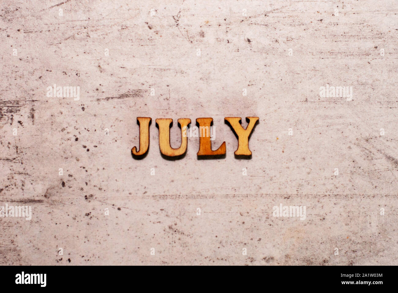 The word July laid out in wooden letters on a light background. Close ...