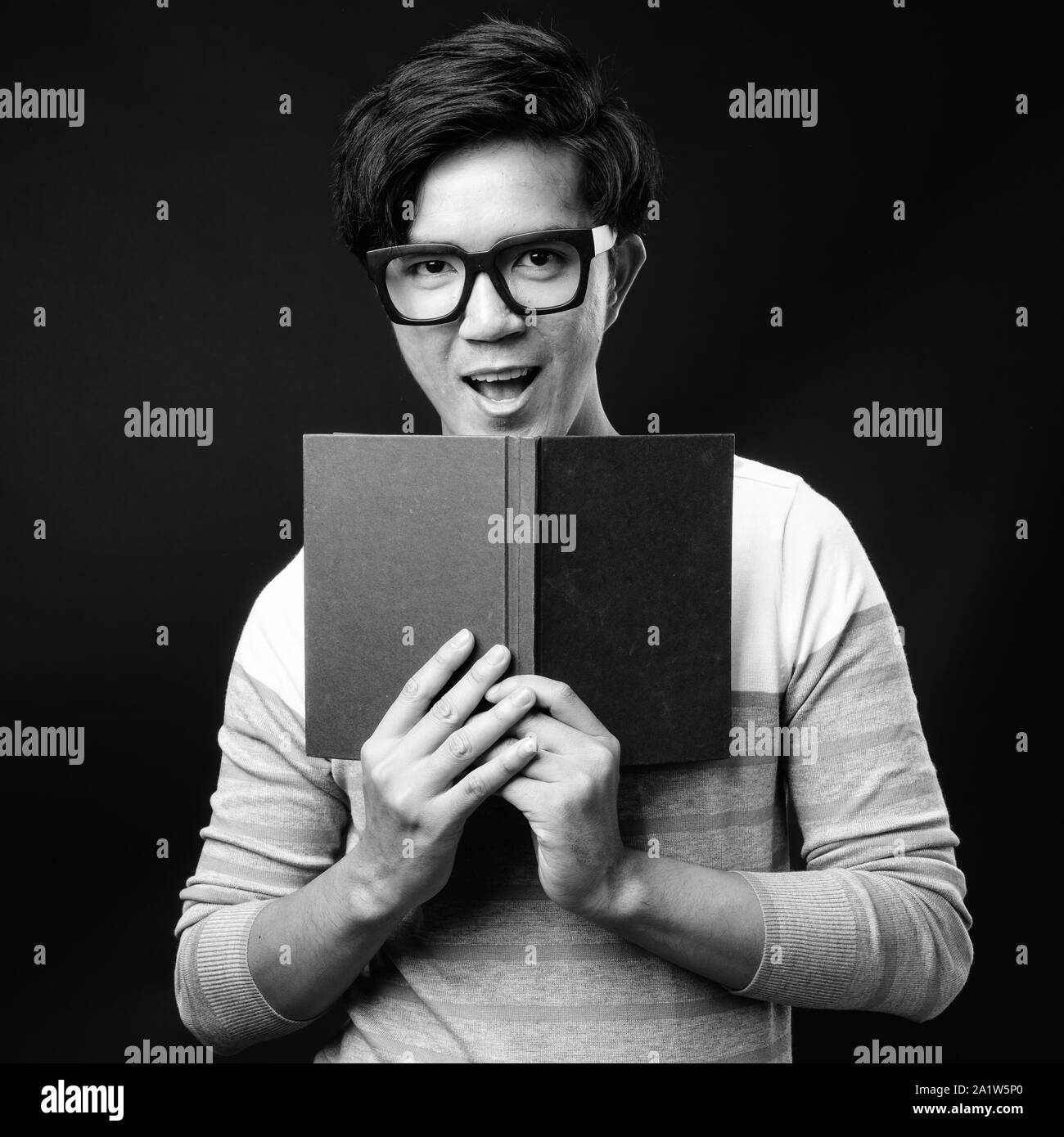 Young handsome Asian man holding diary book against black background ...