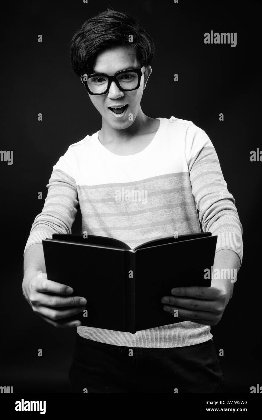 Young handsome Asian man holding diary book against black background ...