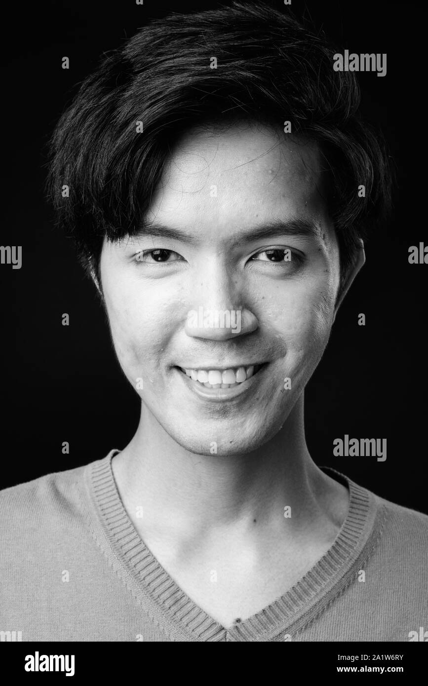 Young handsome Asian man smiling against black background Stock Photo ...