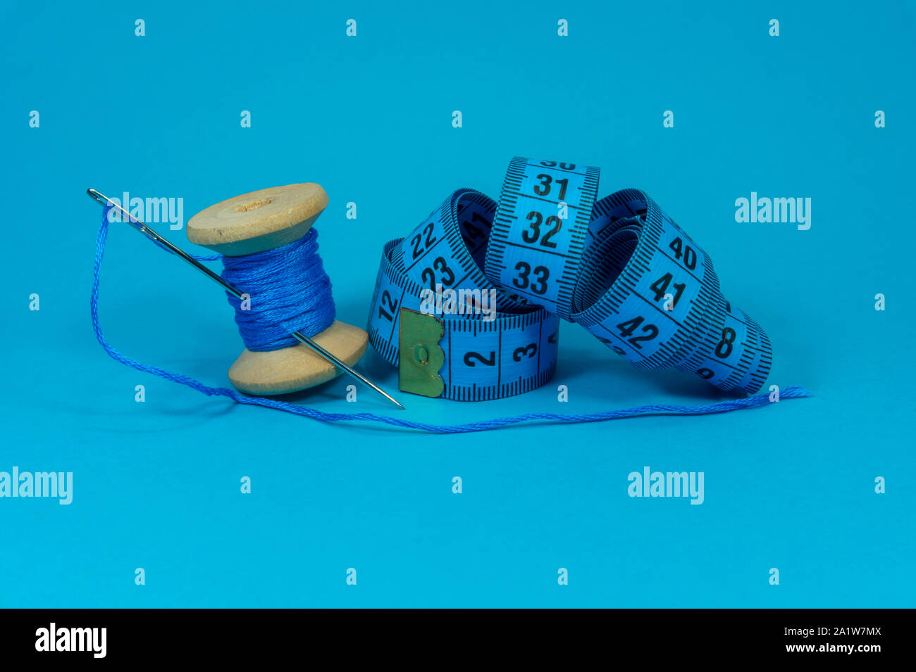 A close up image of a tape measure, spool of blue thread and sewing ...